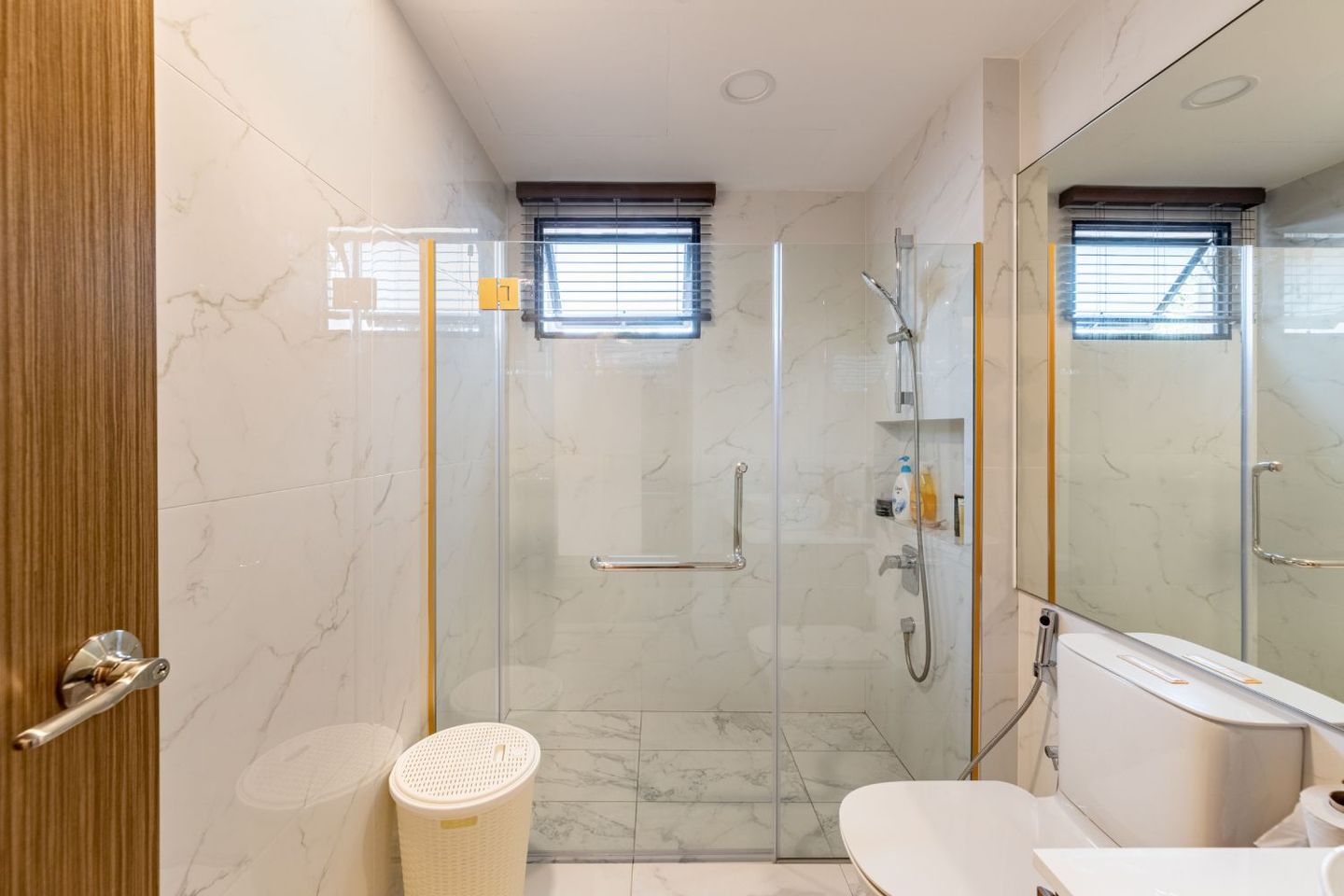 Spacious All-White Bathroom Design With Wooden Vanity Unit And Glass Partition | Livspace